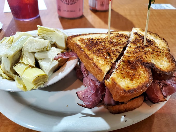 The pastrami sandwich arrives like a meaty monument, flanked by artichoke hearts—a reminder that sometimes the simplest pleasures are the most profound.
