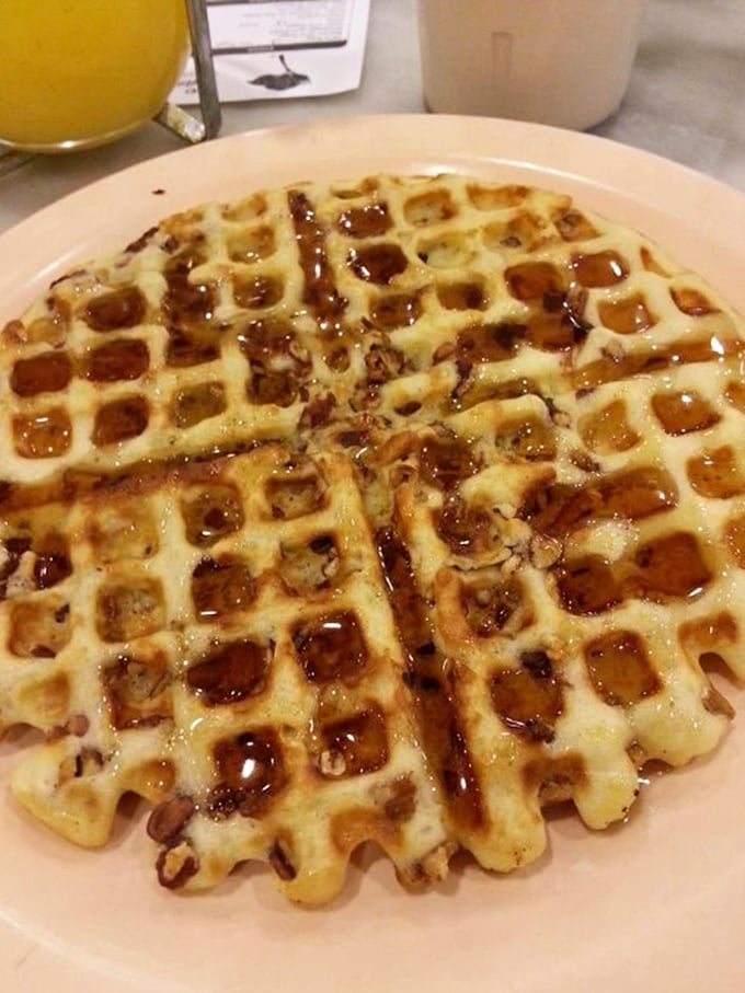 Behold the pecan waffle in its natural habitat—golden, crisp, and absolutely swimming in syrup, like breakfast wearing its Sunday best.