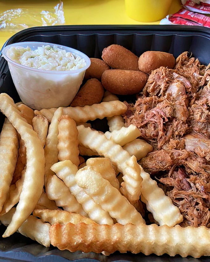 The barbecue trifecta – pulled pork, crispy fries, and hush puppies with slaw – a Southern symphony on a single tray.