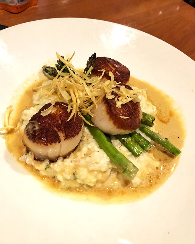 Perfectly seared scallops nestled on creamy risotto with asparagus—proof that seafood this far from an ocean can still make waves.