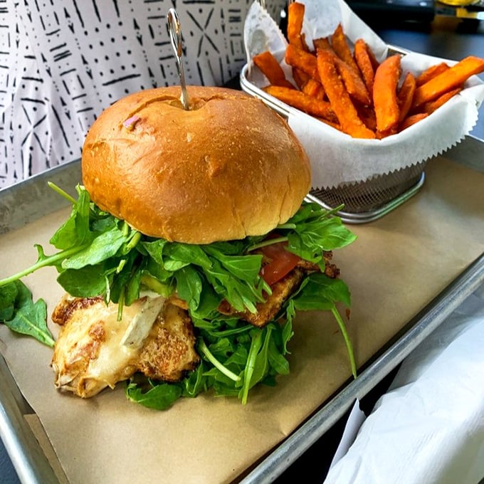 A burger masterpiece that demands your full attention – crisp arugula cascading over a perfectly seared patty, with sweet potato fries standing by for backup duty.