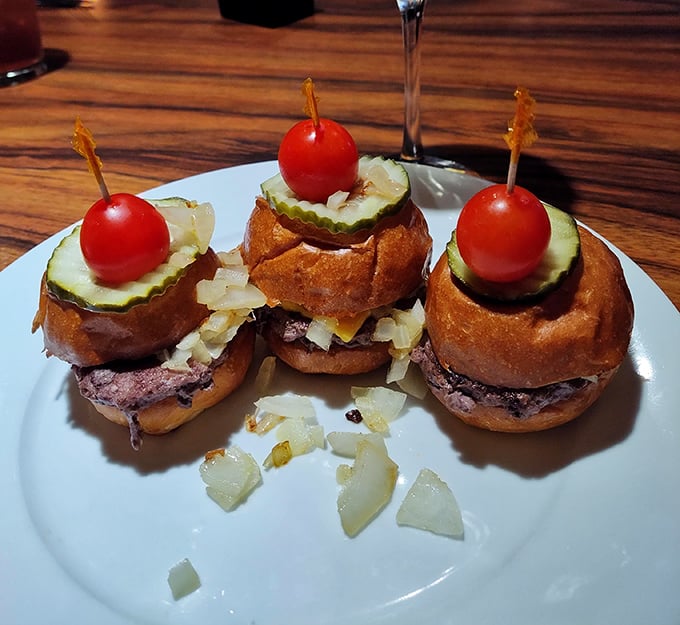 These aren't just sliders – they're miniature flavor bombs, each one topped with a cherry tomato like a tiny edible party hat.