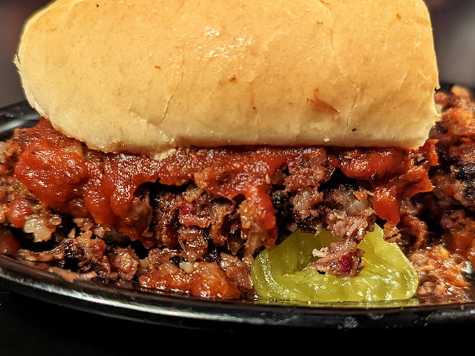 Not your cafeteria Sloppy Joe—this is barbecue royalty dressed casually, sauce-soaked meat cradled by a humble bun with pickle sentinels standing guard.