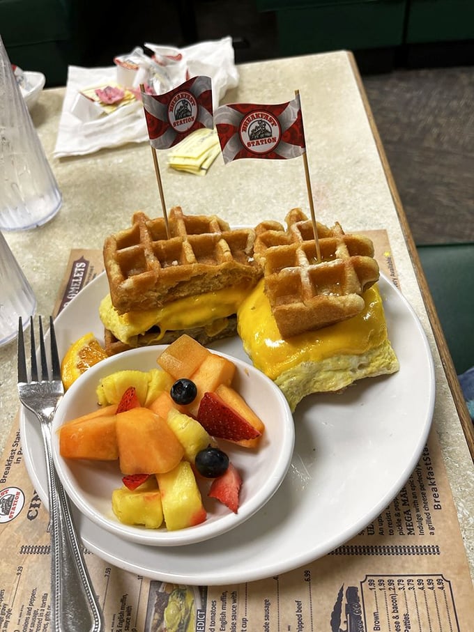 The breakfast sandwich reimagined: eggs and cheese nestled between golden waffles, complete with tiny victory flags. This is breakfast architecture that deserves its own blueprint.