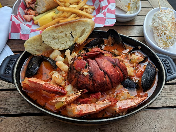 A cast-iron skillet of seafood symphony—lobster tail conducting an orchestra of shrimp, mussels, and potatoes in a tomato-based broth.