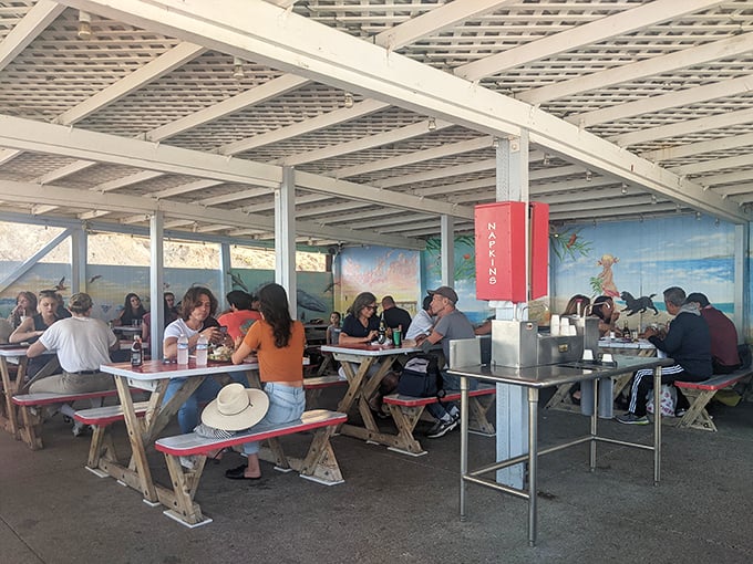 The covered patio fills with happy diners sharing stories and seafood. Notice the hat on the bench—smart visitors come prepared for sun and serious eating.