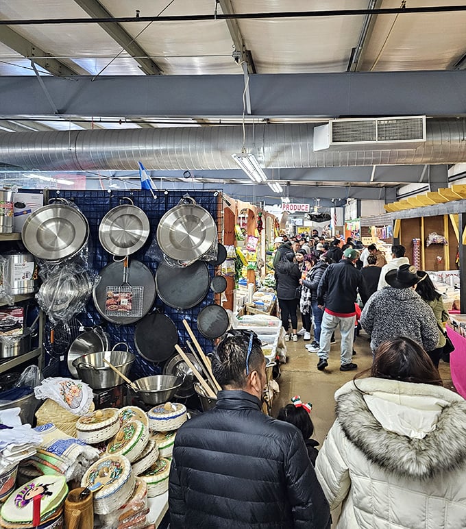 The narrow pathways of commerce! Shoppers navigate this indoor bazaar where professional-grade cookware dangles like kitchen jewelry above the crowd.