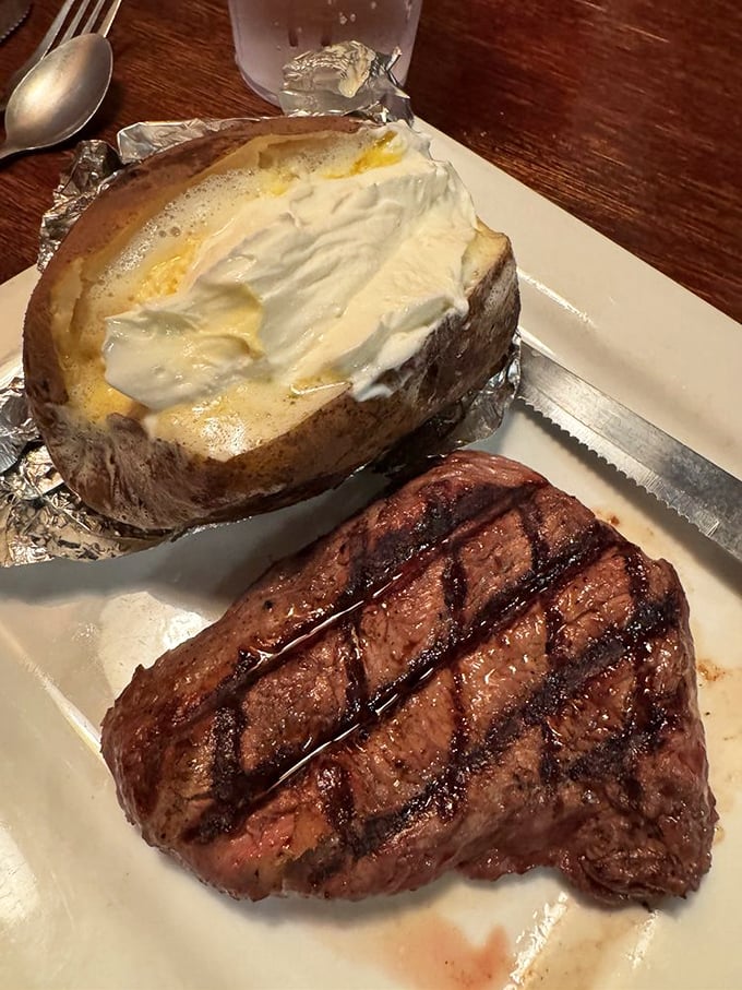A baked potato loaded like a freight train next to a steak with grill marks so perfect they deserve their own geometry lesson.