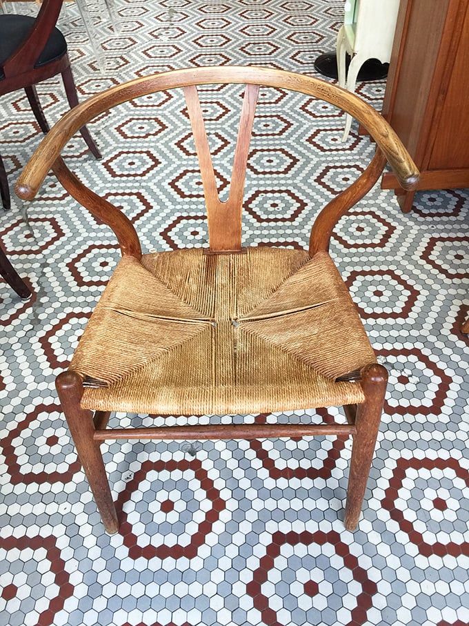 The iconic wishbone chair with its woven seat sits atop a geometric tile floor—a masterclass in timeless design that still feels fresh today.