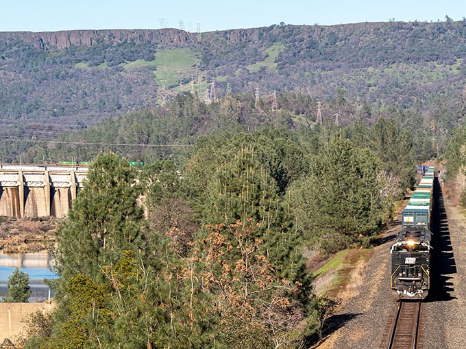 Iron horse meets concrete giant! Oroville's rugged landscape showcases California's industrial ballet – no expensive theater ticket required.