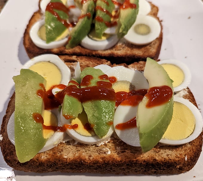 Avocado toast that's actually worth skipping the mortgage payment for—topped with perfectly halved eggs and a zigzag of sauce for good measure.