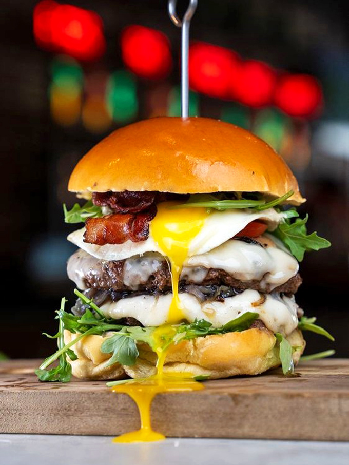 This towering achievement of burger engineering features a runny egg that's basically saying, "Go ahead, get messy – the best meals require extra napkins."