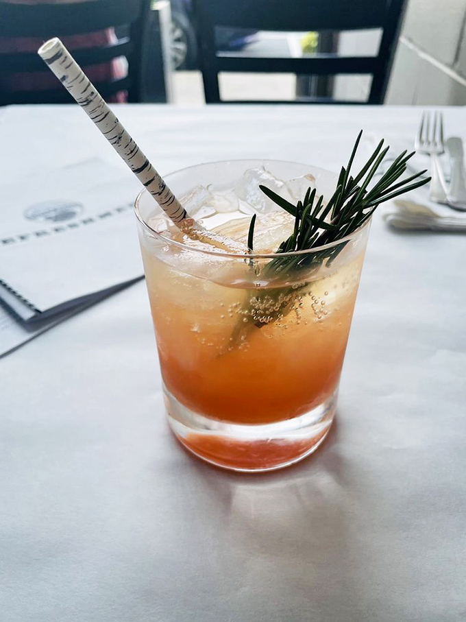 A cocktail garnished with rosemary that looks like it should be sipped slowly while contemplating life's greatest mysteries—or at least tonight's dessert options.