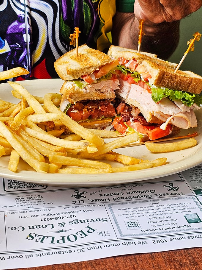 The club sandwich—America's three-story answer to lunch indecision. Turkey, bacon, and veggies stacked so high they need those little toothpick flags as structural support.