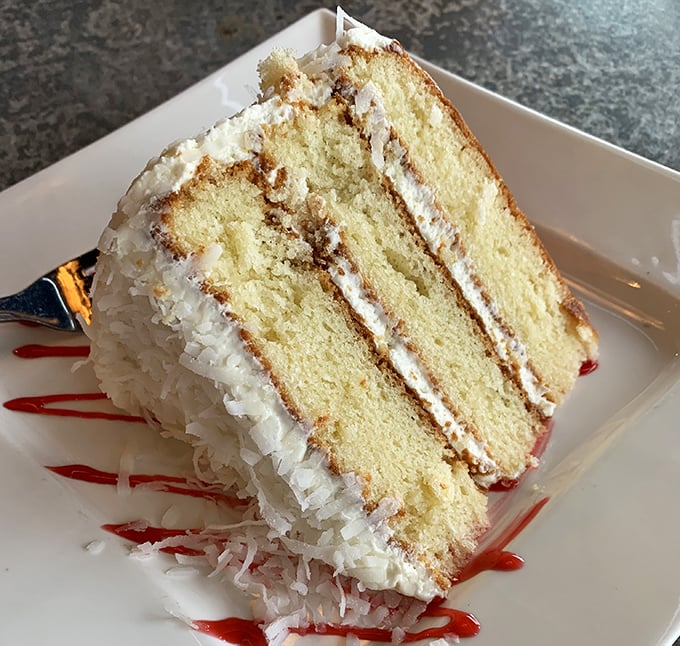 A slice of coconut cake that doesn't whisper "tropical vacation"—it belts it out like a Broadway finale, complete with dramatic raspberry sauce.