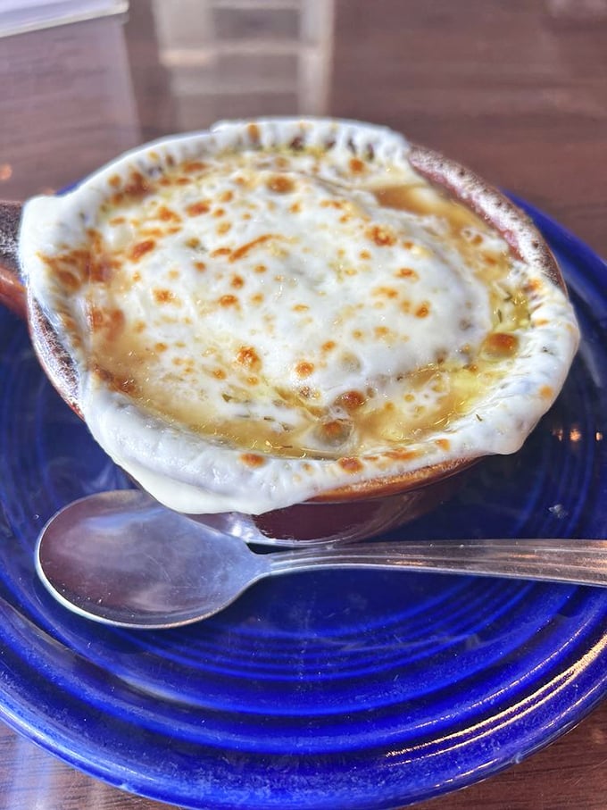 French onion soup wearing its cheese cap with pride—a bubbling masterpiece that's basically an edible hug in a blue ceramic crock.