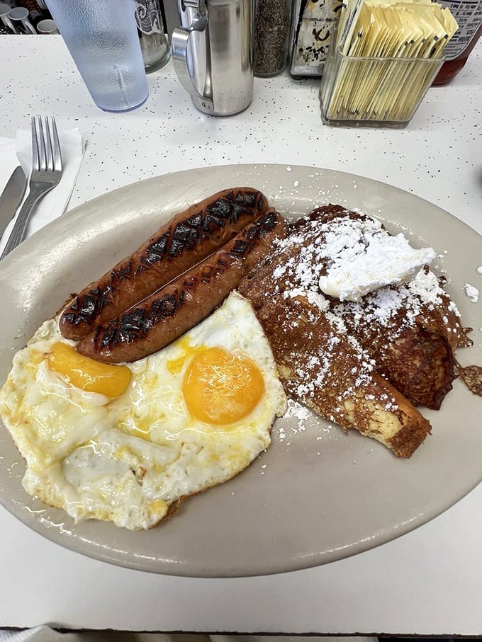French toast and sausage links sharing a plate like old friends at a reunion. The powdered sugar isn't garnish—it's essential punctuation.