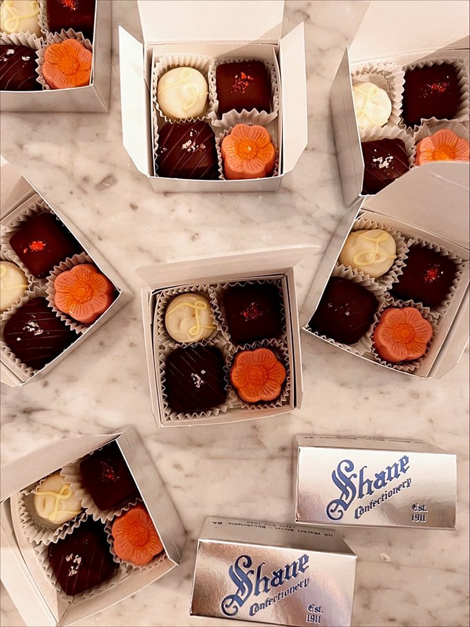 Tiny boxes of artisanal truffles arranged like a marble chess board—a game where every move ends in victory and chocolate-stained fingers are badges of honor. 