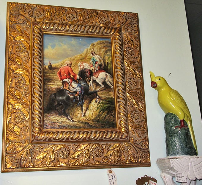 Art meets whimsy as an ornate gold-framed painting shares wall space with a cheerful yellow bird figurine – unexpected neighbors in the antique world.