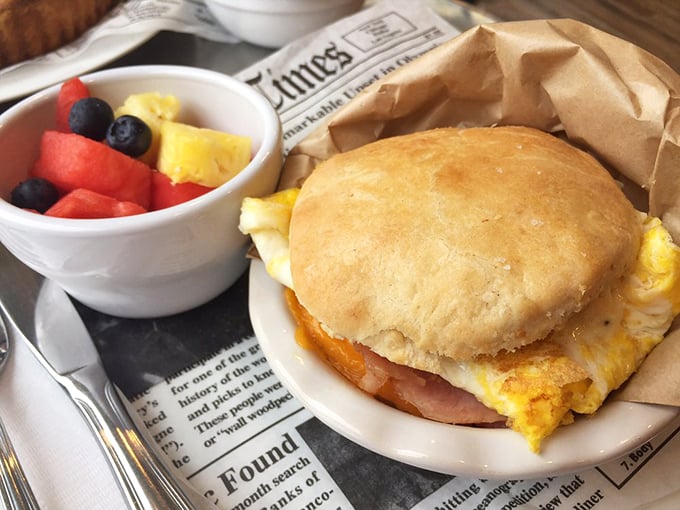 Fluffy biscuit cradling eggs and ham alongside fresh fruit—breakfast sandwiches elevated to art form status here.