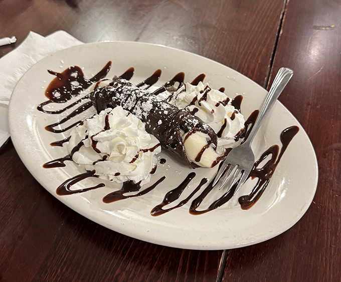 The cannoli—that magical tube where crispy pastry meets creamy filling—sits drizzled with chocolate like it's dressed for the dessert equivalent of the Met Gala.