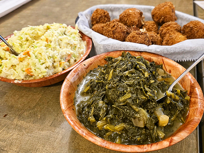 Coleslaw and turnip greens in wooden bowls alongside golden hushpuppies—side dishes that refuse to be upstaged by the main event.
