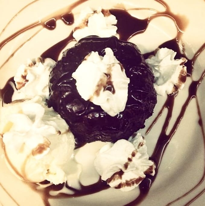 A chocolate dessert surrounded by whipped cream islands and chocolate sauce rivers. Diet plans come here to die happy and without regrets.