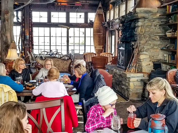 The dining room feels like your outdoorsy uncle's dream living room – stone fireplace, vintage canoes, and windows framing nature's own watercolor.