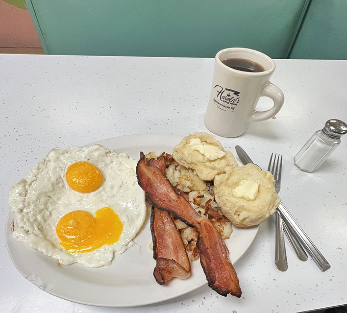 Two sunny-side-up eggs with perfectly crisp bacon and homemade biscuits—proof that simplicity, when done right, is the ultimate sophistication.