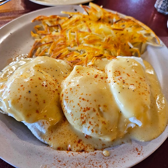 Eggs Benedict done diner-style – perfectly poached eggs nestled on English muffins, blanketed in hollandaise with crispy hash browns standing guard.
