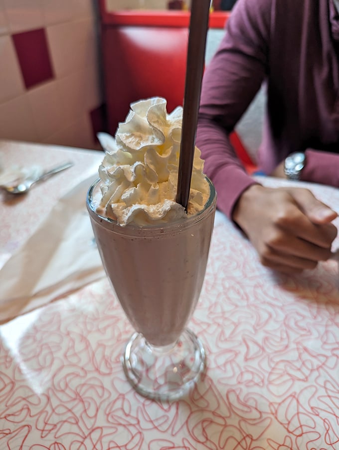 This chocolate milkshake topped with whipped cream towers over its glass like a delicious architectural achievement worth celebrating.