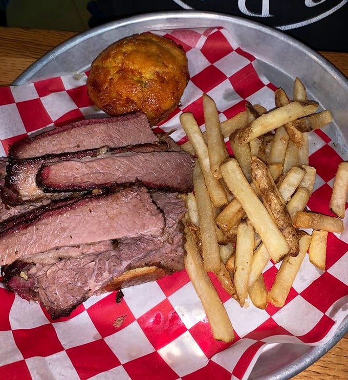Brisket sliced with the precision of a surgeon, revealing that coveted pink smoke ring – evidence of the 14-hour hickory smoking process that transforms tough cuts into meat butter.
