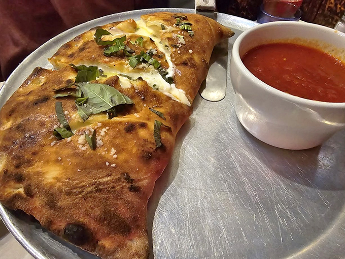 The calzone – pizza's mysterious, introverted cousin – arrives with a side of marinara for necessary dipping adventures.