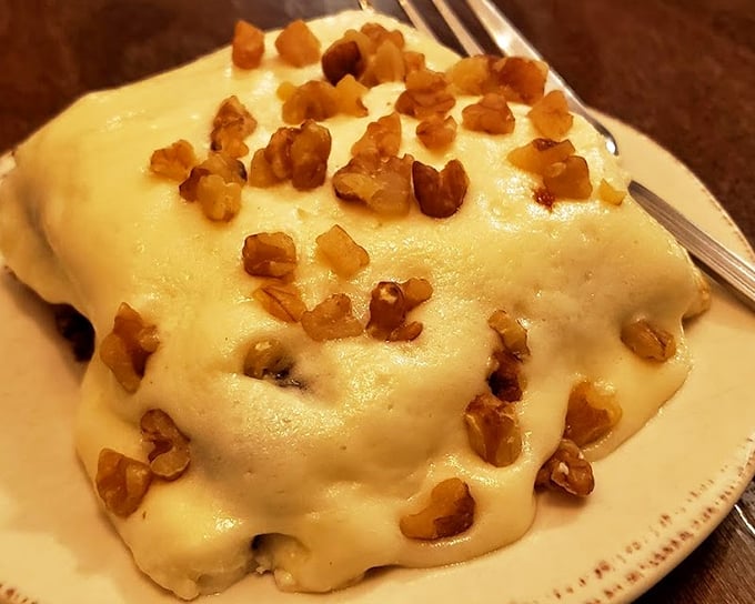 This isn't just dessert, it's therapy—creamy cake topped with what appears to be cream cheese frosting and crunchy nuts for textural perfection.