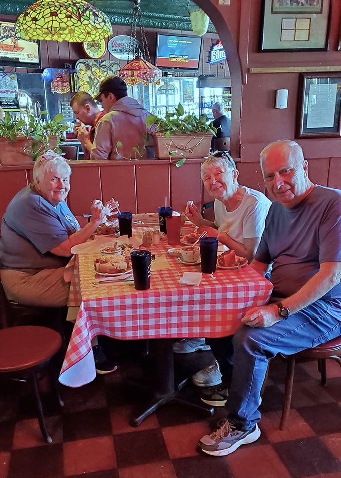 Happy diners gathered around red checkered tablecloths—the universal signal that you're about to enjoy food that prioritizes flavor over pretension.