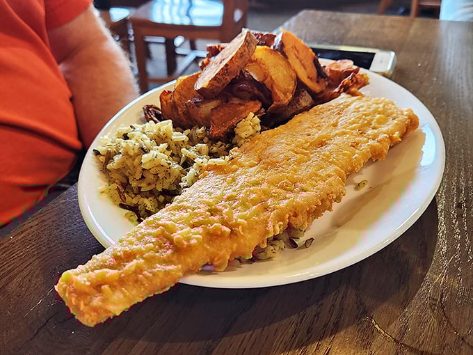 A fish fillet so generously sized it barely fits the plate, flanked by wild rice and vegetables.