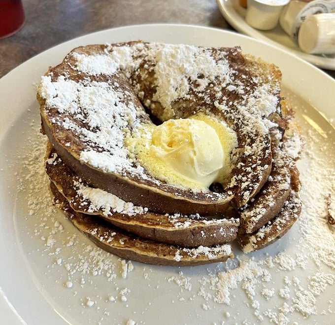French toast stacked higher than your weekend expectations, dusted with powdered sugar like fresh snow on delicious mountains.