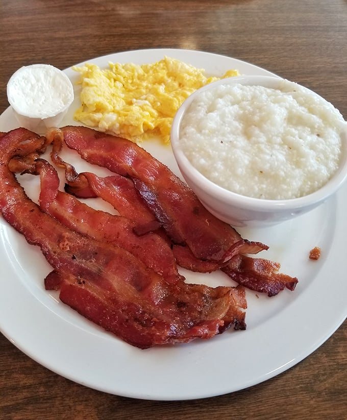 The breakfast trinity: crispy bacon, fluffy eggs, and creamy grits—proof that sometimes the simplest combinations create the most profound satisfaction.