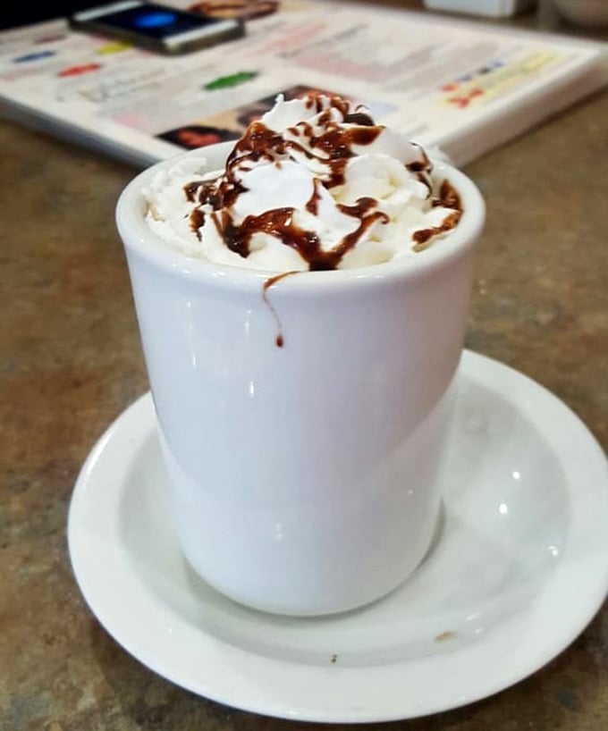 Hot chocolate that understands its assignment: whipped cream mountain, chocolate drizzle rivers, and a mug substantial enough to warm winter-chilled hands.