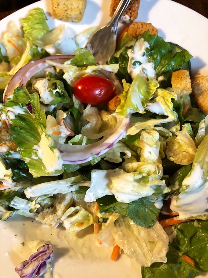 Even the salad looks happy to be here – crisp lettuce, veggies, and croutons playing nicely together under a light drizzle of house dressing.