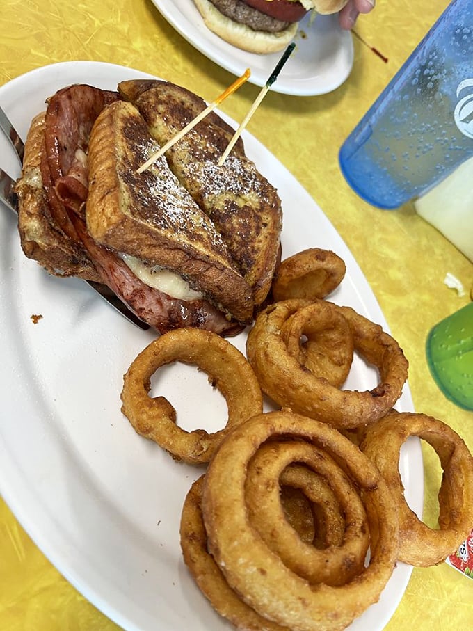 The Monte Cristo sandwich—where French toast meets ham and cheese in a powdered sugar love affair, with onion rings playing perfect wingman.