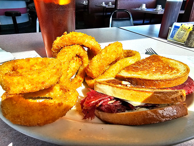 The Reuben sandwich stands tall and proud, flanked by onion rings so perfectly golden they deserve their own Instagram account.