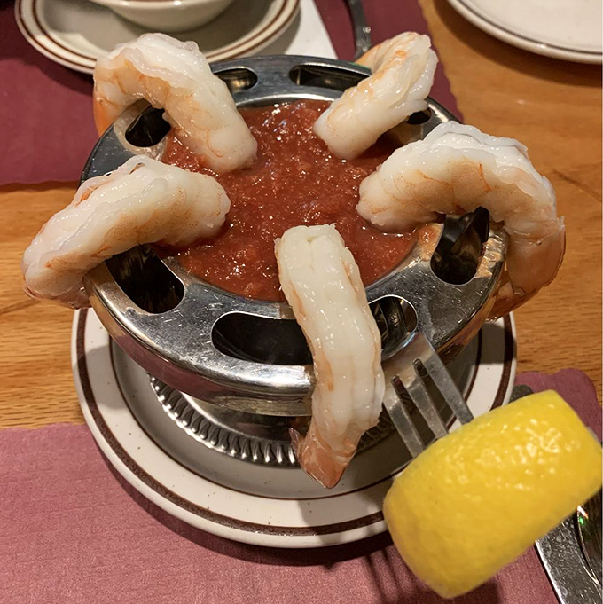 The classic shrimp cocktail—five plump sentinels standing guard around a pool of tangy sauce, a timeless appetizer that never goes out of style.