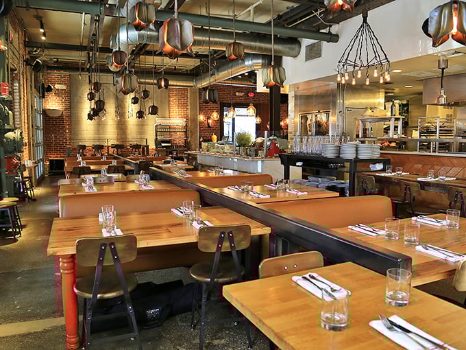 Wooden tables, leather booths, and copper pendant lights create a dining room where industrial meets intimate—like a hug in warehouse form.