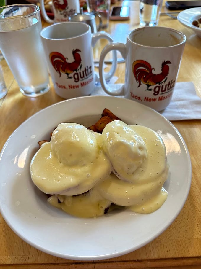 Eggs Benedict gets the Gutiz treatment with hollandaise so perfect it deserves its own fan club. Those branded mugs in the background are souvenirs waiting to happen.