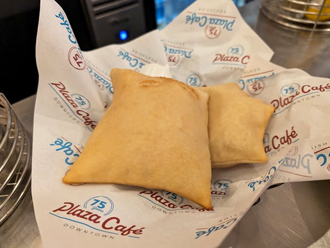 Sopaipillas nestled in branded paper—puffy pillows of fried dough waiting to be drizzled with honey and devoured without shame.